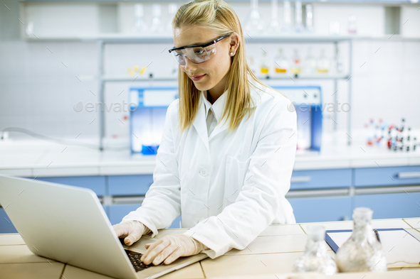 Cute female researcher in white lab coat and protective goggles using ...