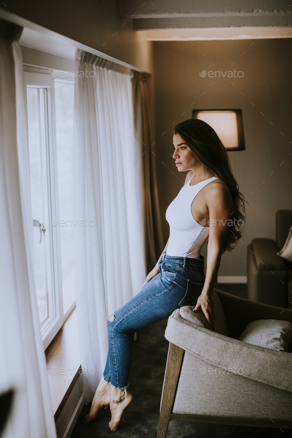 Beautiful young woman sitting by the window Stock Photo by BGStock72