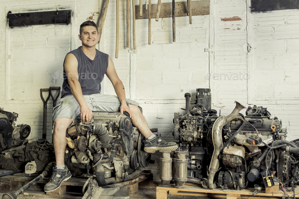 Mechanic sitting on a car engine with multiple engines around it. Stock ...
