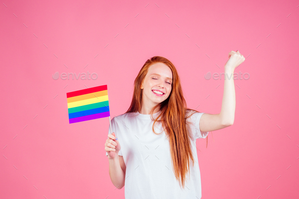 redhaired ginger woman holding colorful flag in studio pink background ...