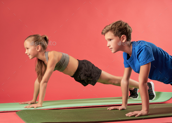 Adorable girl and boy doing plank against red background Stock Photo by ...