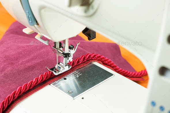 Modern sewing machine presser foot and decorative edging cord on red ...