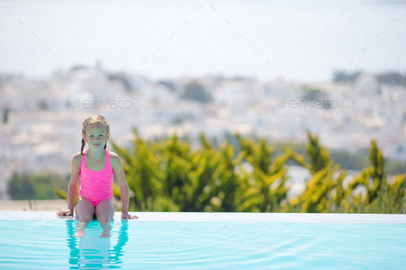 Adorable little girl on the edge of outdoor swimming pool with ...