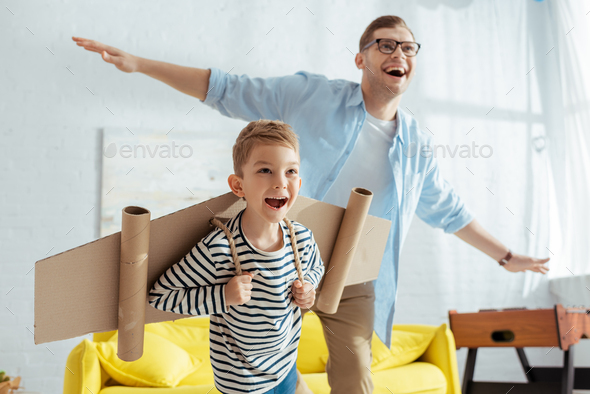 happy boy with carton plane wings, and cheerful father having fun while ...
