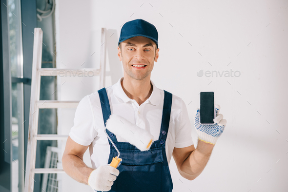 handsome young painter in uniform holding paint roller and showing ...