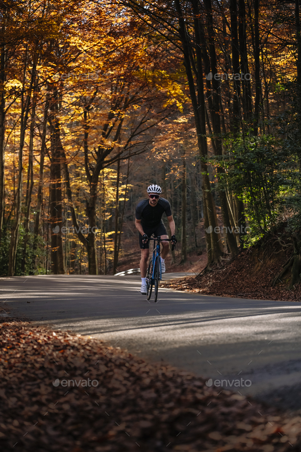 Cyclist riding a bike on a curved road in autumn scenery Stock Photo by ...