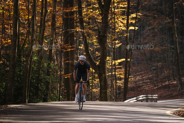 Cyclist riding a bike on a curved road in autumn scenery Stock Photo by ...