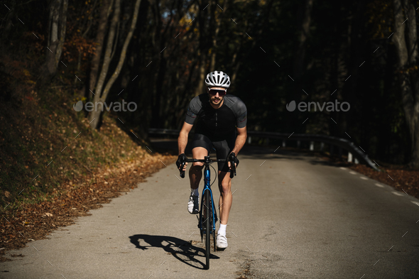 Cyclist riding a bike on a curved road in autumn scenery Stock Photo by ...