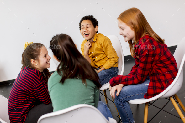 Portrait of cute little kids in jeans talking and sitting in chairs ...