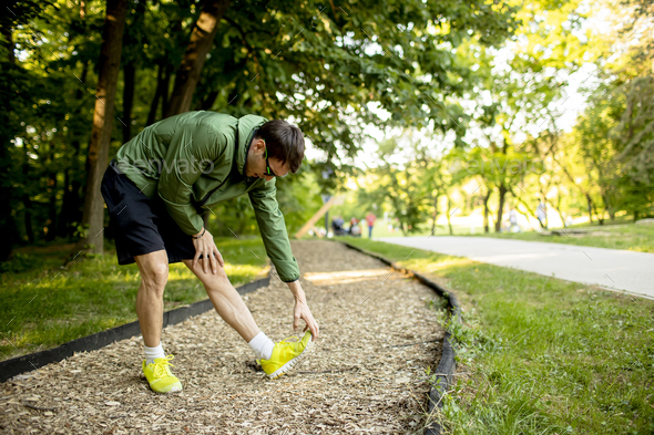 Athletic young man having a break while doing workout in sunny green ...