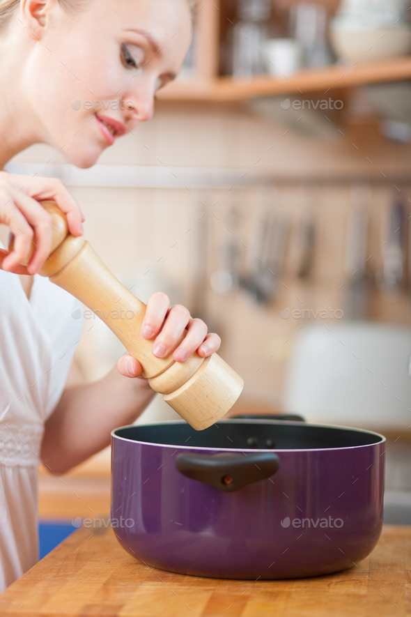 young woman cooking in the kitchen- adding salt and pepper into the pot ...
