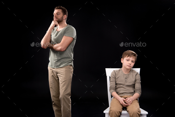 Father standing with hand on chin and upset little boy sitting on stool ...