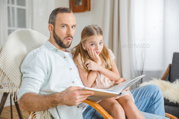 Scared father and daughter sitting in rocking chair and reading book ...