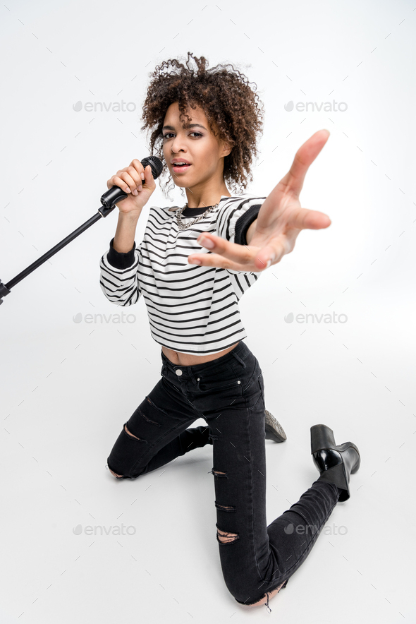Beautiful young kneeling woman with microphone singing and gesturing ...