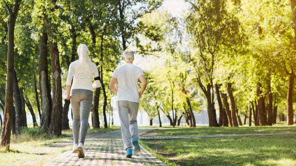 Full length back view of healthy mature couple jogging in park at early ...