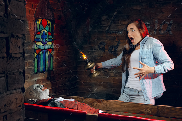 Frightened girl with lamp in hand screaming over coffin with vampire ...