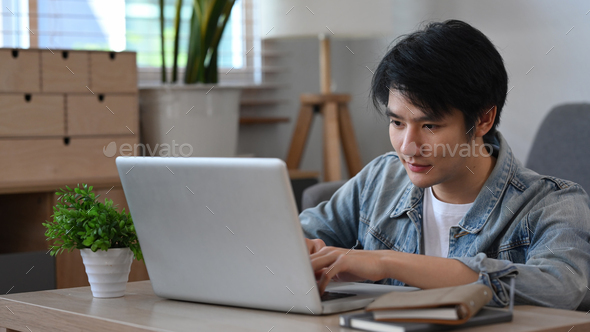 Handsome asian man sitting in living room and browsing internet with ...