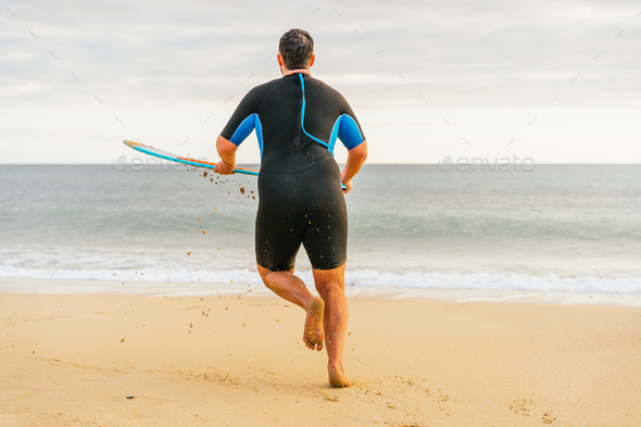 Caucasian hispanic man running down the beach to catch a wave with a ...