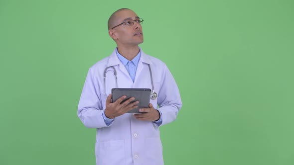 Happy Bald Multi Ethnic Man Doctor Thinking While Using Digital Tablet ...