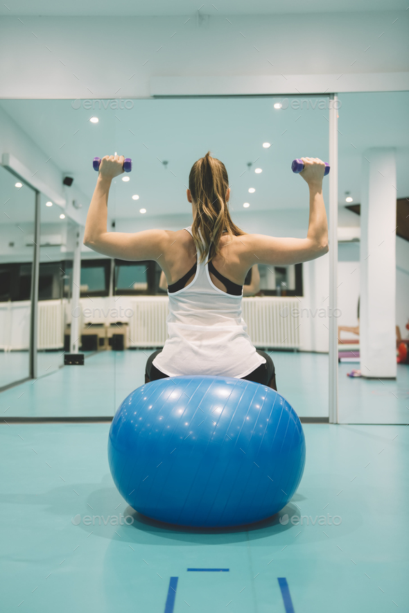 Young girl in sports suit does physical exercises with dumbells and a ...