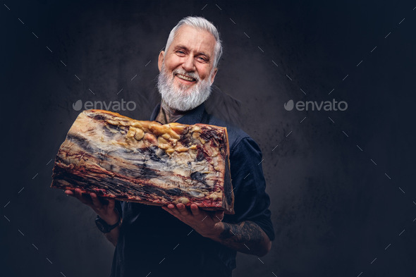 Joyful elderly butcher with apron holding huge meat piece Stock Photo ...