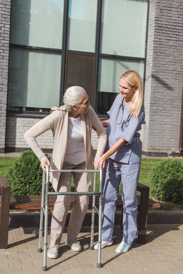 nurse and senior patient with walker smiling each other outside nursing ...