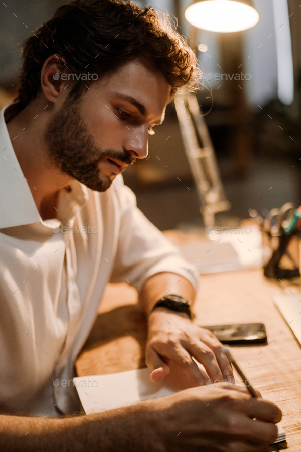 White man writing down notes in planner while working at office Stock ...
