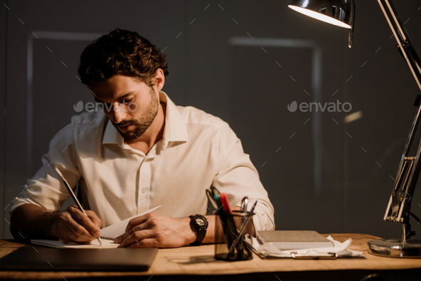 White man writing down notes in planner while working at office Stock ...