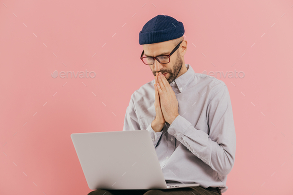 Male programmer keeps hans in praying gesture, looks at screen of ...