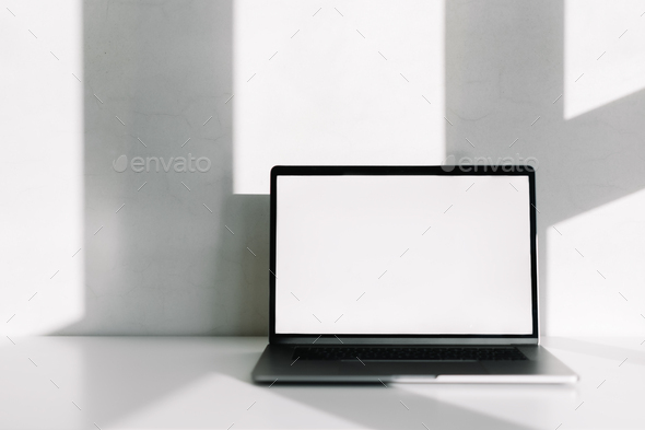 Laptop computer with white blank screen on the white table with shadow ...