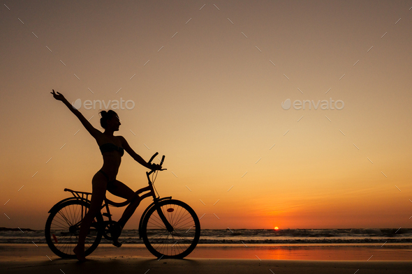 healthy alone woman ride on bicycle on empty sunset Goa India beach ...