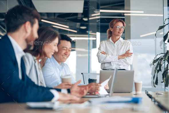 Smiling confident female boss looking at side on business meeting with ...