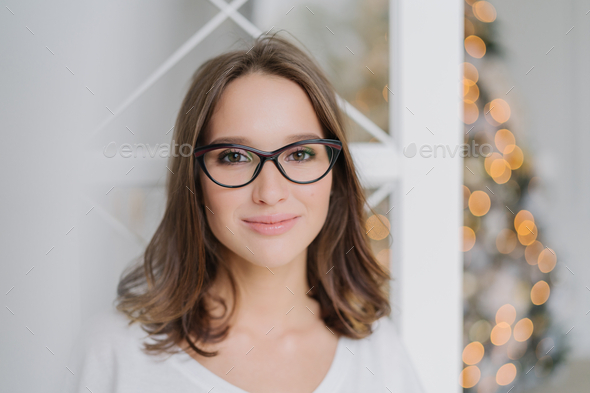 Female wears spectacles for good vision, looks happily at camera, has ...