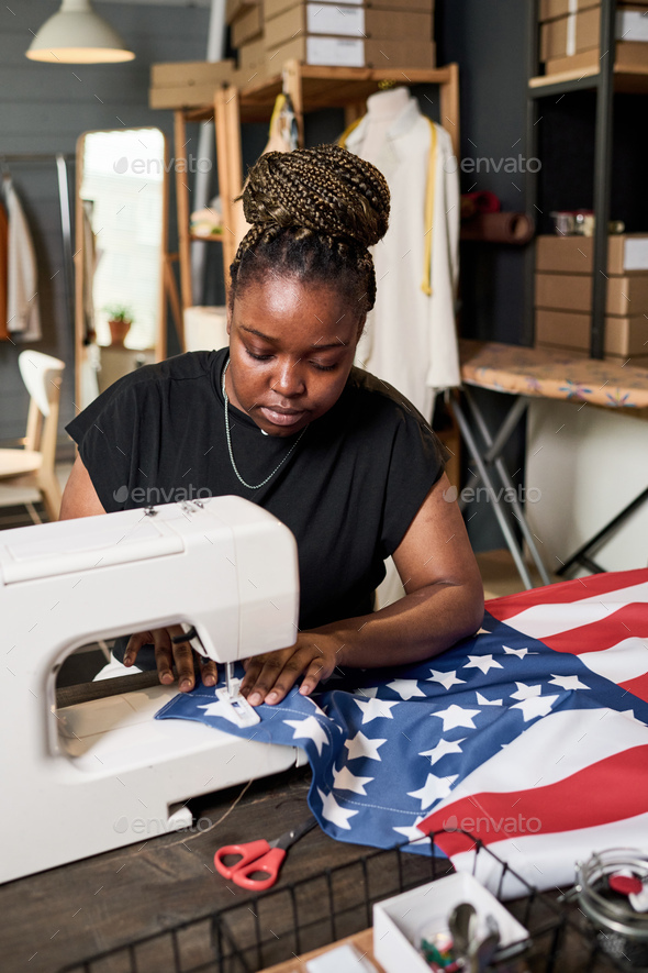Young serious black woman sewing American flag by large table in ...