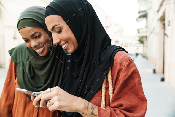 Multiracial muslim women using mobile phone on city street Stock Photo ...