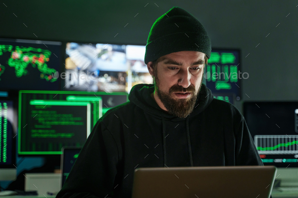 Male hacker with beard working near computer monitors with data on ...