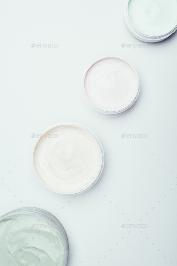 flat lay with different clay masks in containers placed in row isolated ...