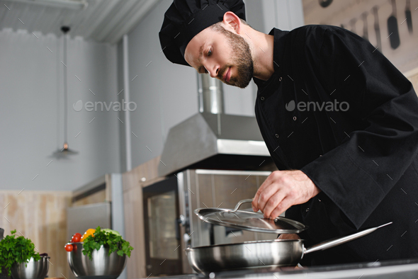 side view of handsome chef cooking with frying pan at restaurant ...