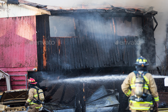 Firefighter sprays water on burning house fire Stock Photo by MatHayward