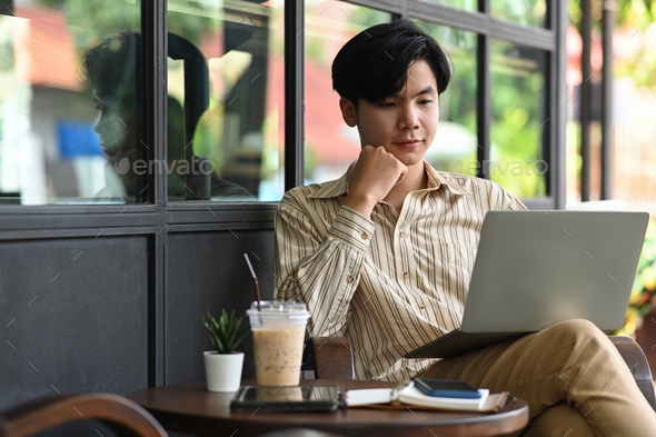 Handsome Asian man sitting outdoor cafe and working with laptop ...