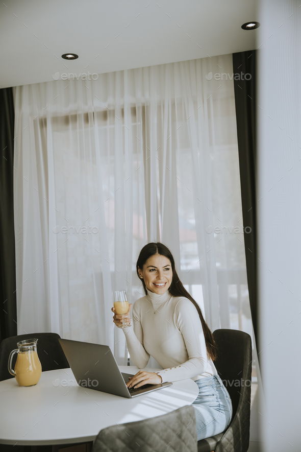 Young woman using a laptop computer and drinking healthy orange juice ...
