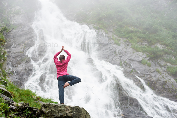 Young girl in a yoga pose near powerful waterfall. Stock Photo by ...