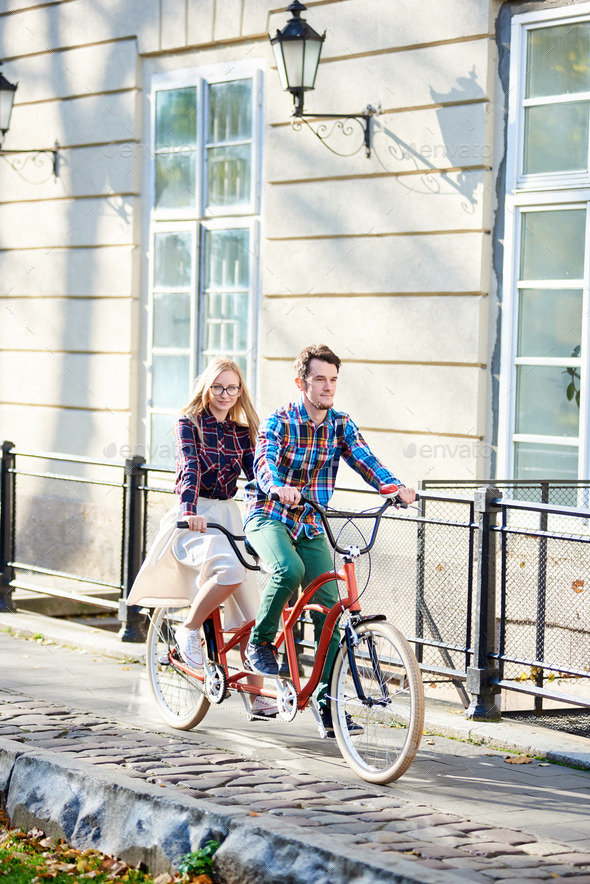 Young tourist couple, handsome man and pretty blond woman riding tandem ...