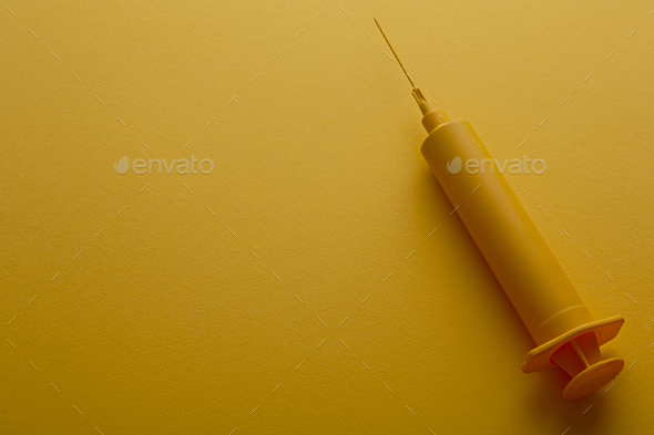 Yellow injection syringe on yellow background. Stock Photo by jgcocinarte