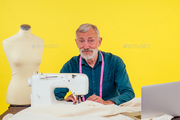 pleasing old man working in tailoring studio making clothes at sewing ...