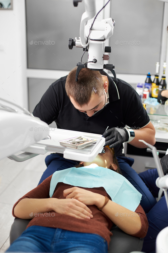 Dentist is treating the patient's teeth by bending over her in a clinic ...