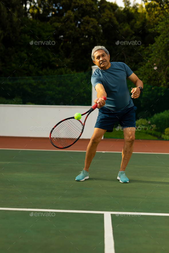 Biracial senior man hitting tennis ball with racket while playing ...