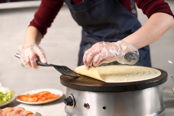Chef hands turn over pancake by spatula on portable cooktop. Baking ...