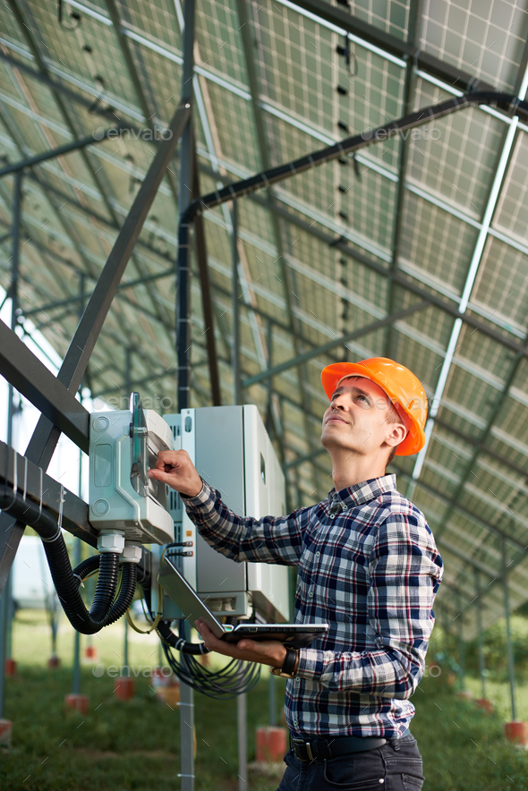 Operator in helmet and with laptop at station checking the operation of ...