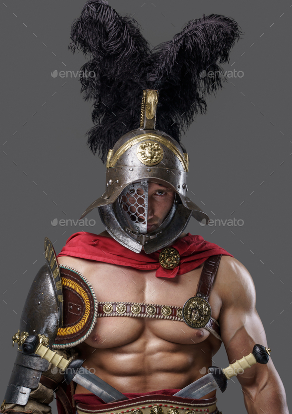 Muscular roman gladiator looking at camera against grey background ...